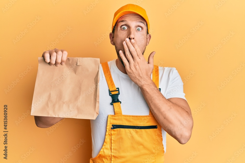 Young handsome delivery man holding take away paper bag covering mouth ...