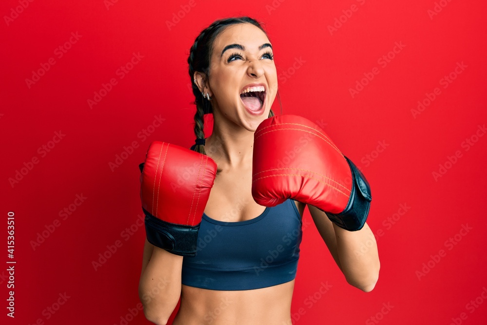Young brunette girl using boxing gloves angry and mad screaming ...