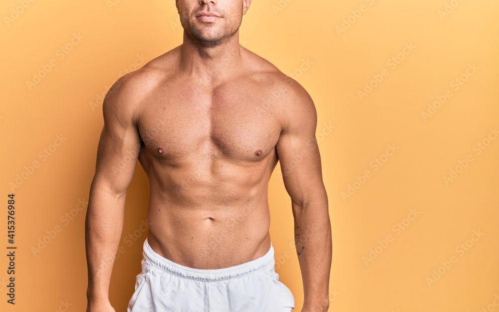 Handsome muscle man standing shirtless with serious expression on face ...