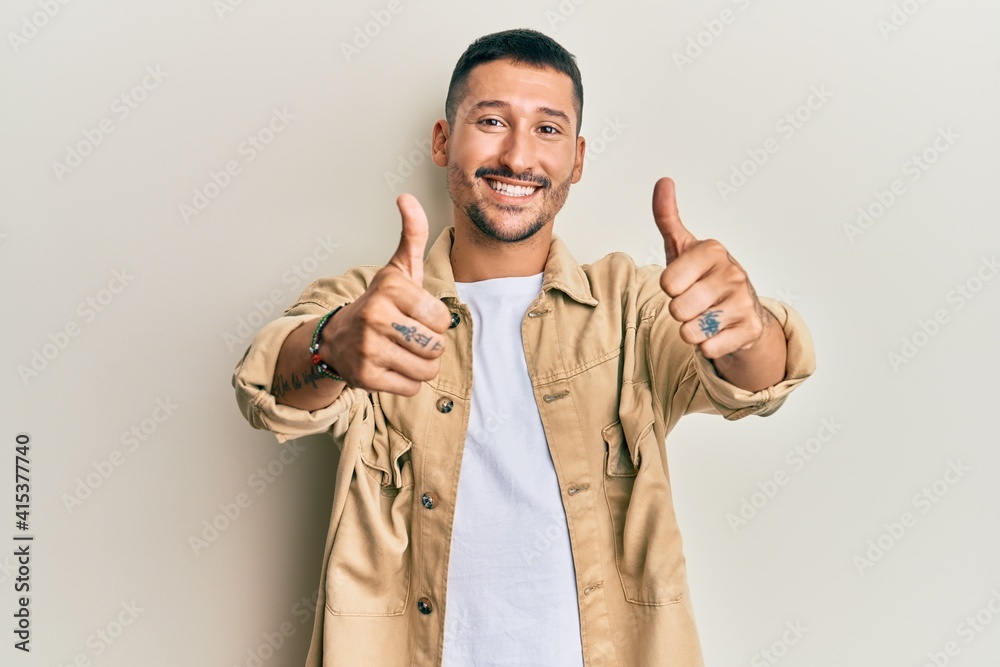 Handsome man with tattoos wearing casual brown denim jacket approving ...