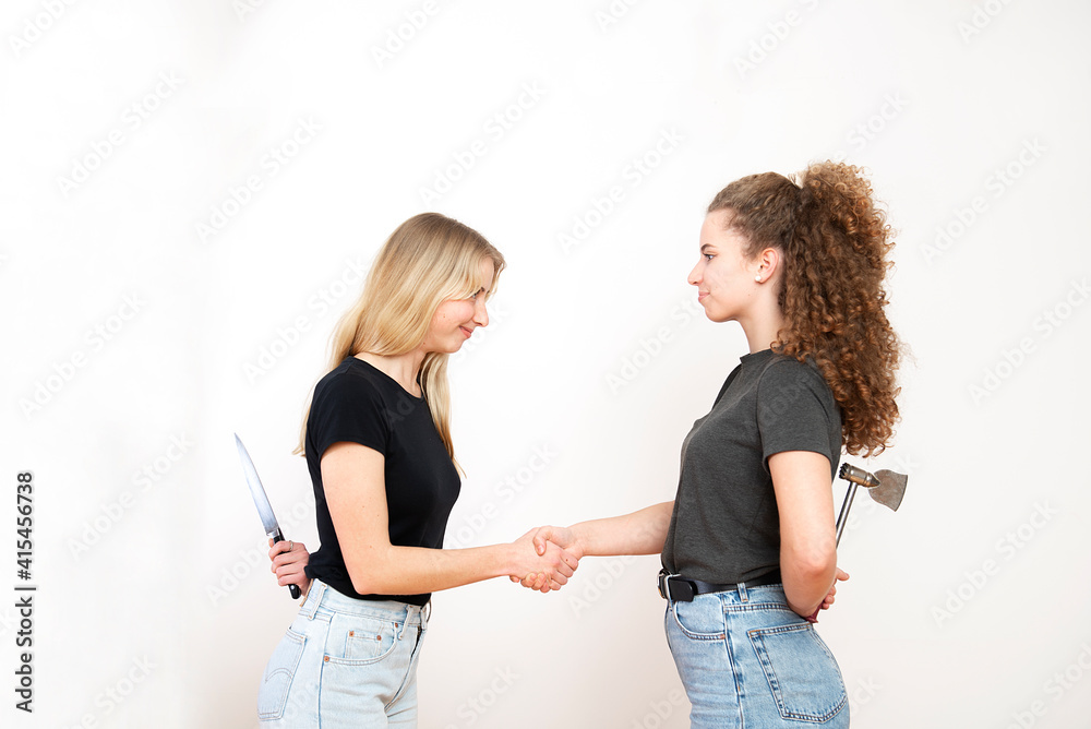two smiling women standing face to face and hiding knife and axe behind ...