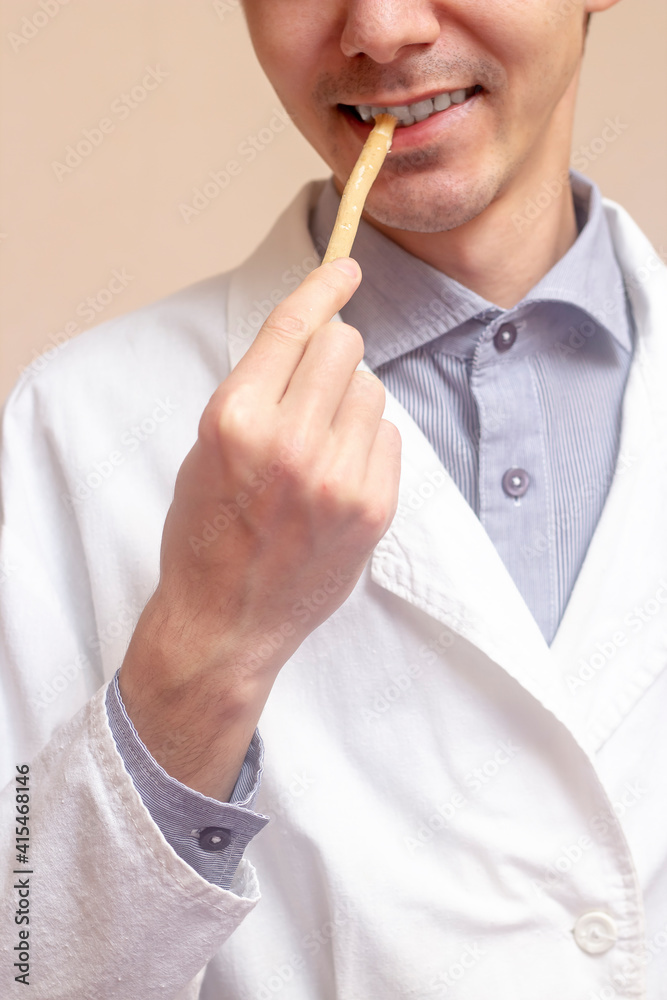 A young man brushes his teeth with a miswak (siwak) in a white coat ...