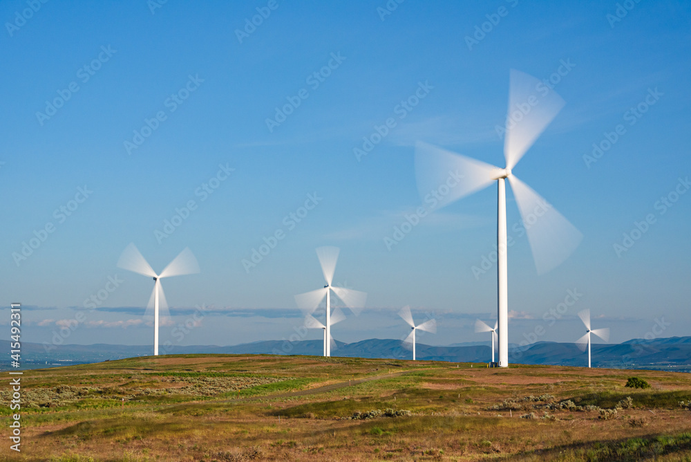 Spinning Wind Turbines against blue sky shown in slow motion to capture ...