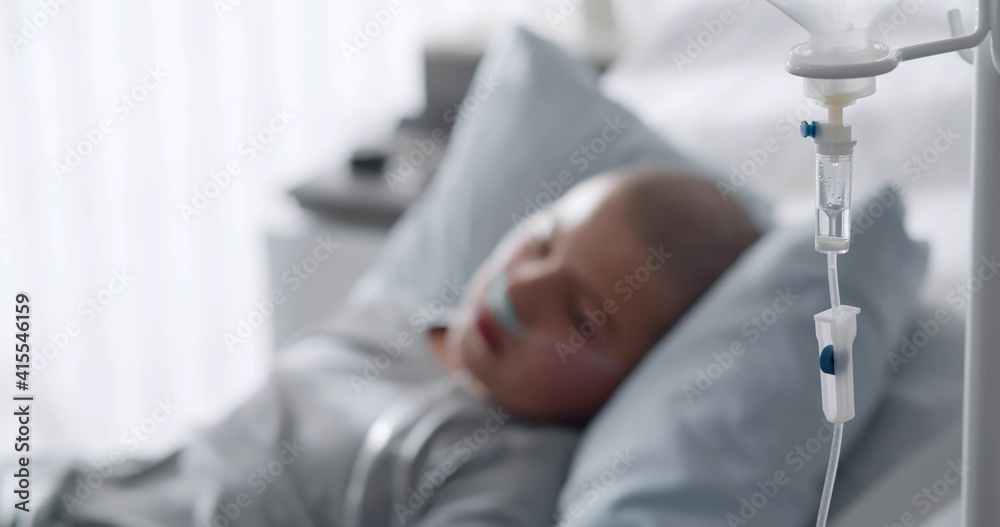 Focus on intravenous drip with sick kid lying in hospital bed on ...