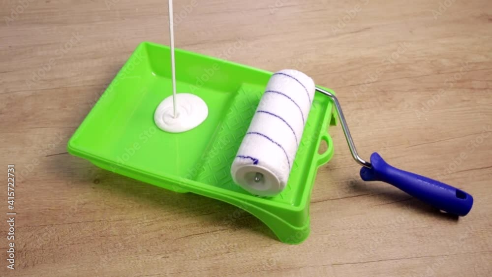 Paint roller with blue handle in a green tray with white paint on a ...