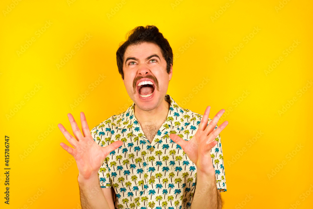 young handsome Caucasian man wearing Hawaiian shirt against yellow wall ...