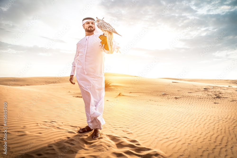 Arabic man with traditional emirates clothes walking in the desert with ...