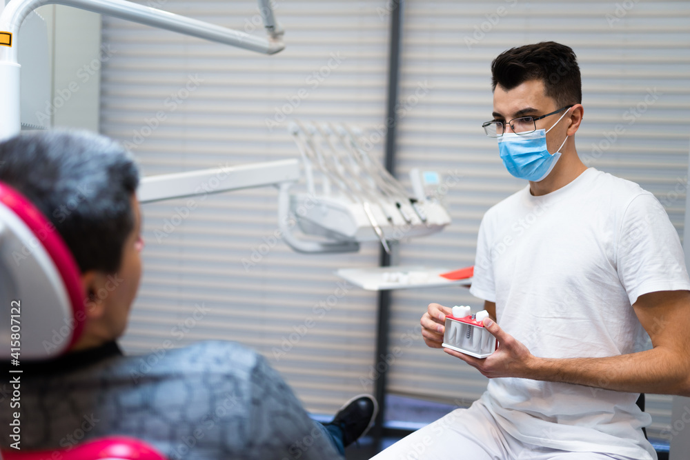 Dental surgeon with dental crown in hands model talks to patient about ...