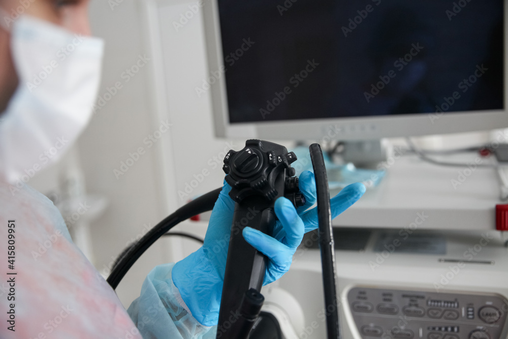 An endoscopist in blue gloves holds an endoscope in his hands. In the ...