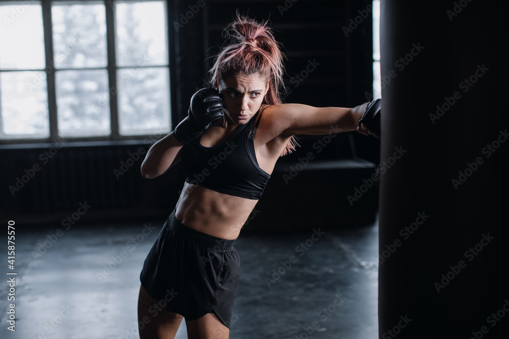 Athletic fit female boxer exercising punches with boxing bag in gym ...
