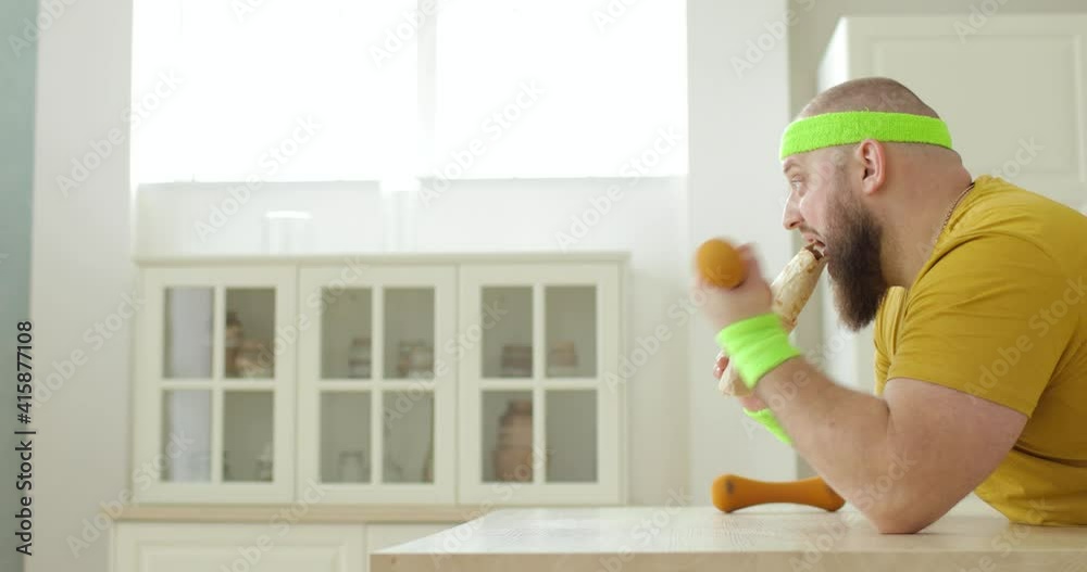 Fat man is eating danar shawarma sitting at table and doing exercise ...