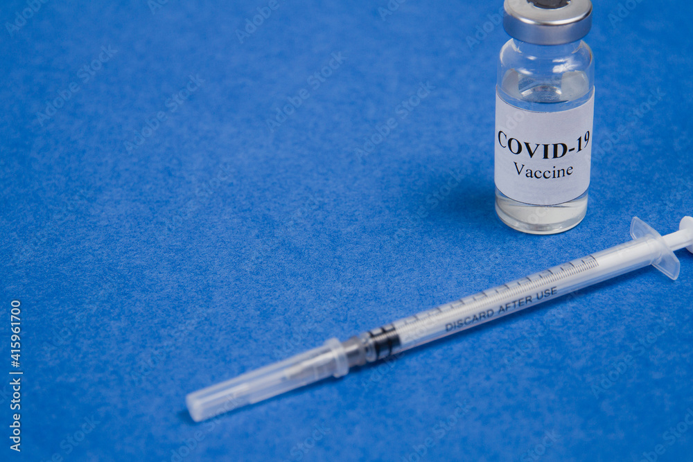 Vial of Covid-19 vaccine and syringe for injection on a blue background ...