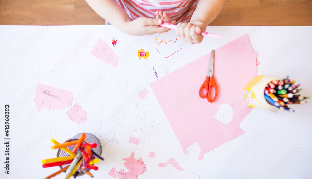 Top view of a child working on her project on the table with scissors ...