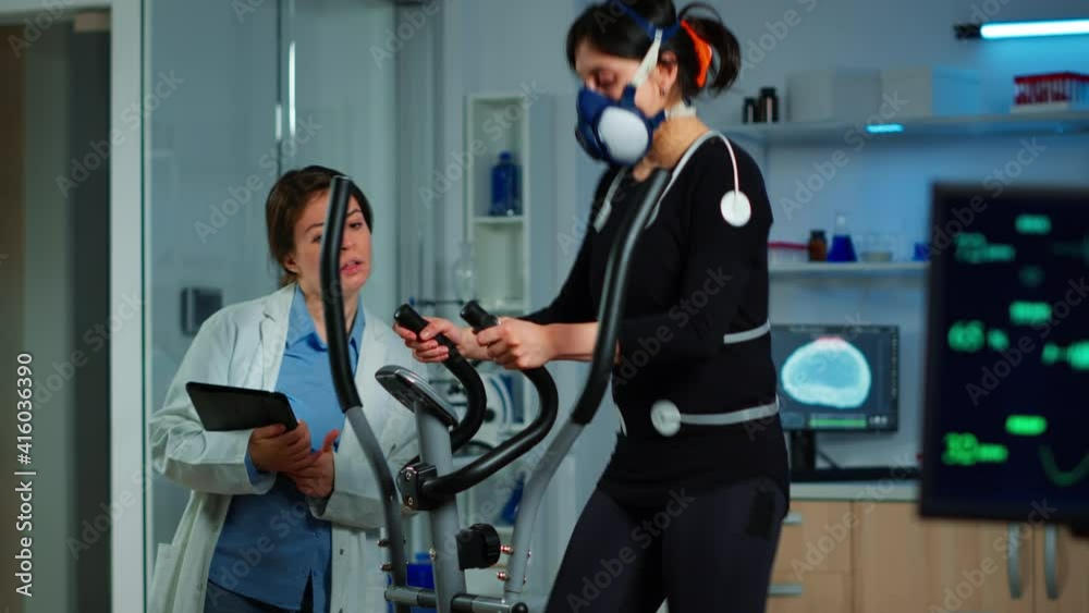 Woman athlete with mask running on cross trainer in sports science lab ...