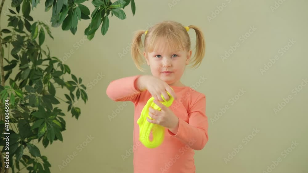 Playful cute little girl standing up and stretching yellow slime to the ...