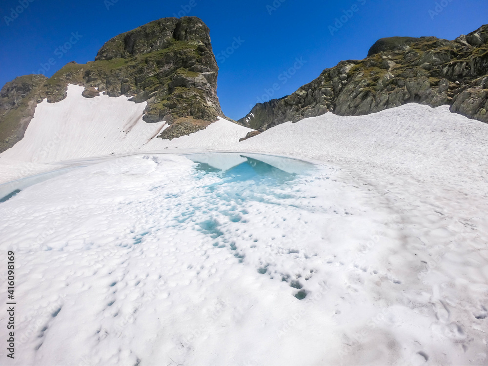A view on a ice-frozen alpine lake. The ice shines in many different ...