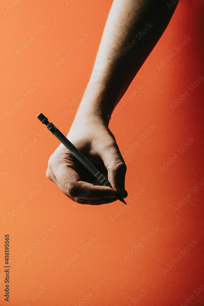 A young hand grabbing a mechanical pencil over a orange background with ...