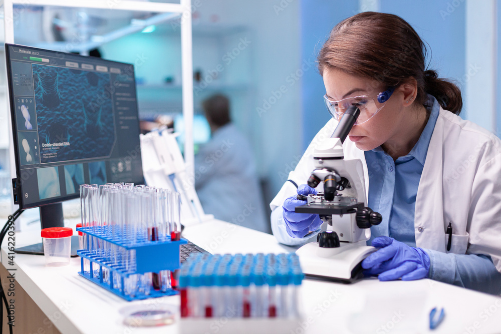 Scientist looking into microscope in virus research laboratory with ...