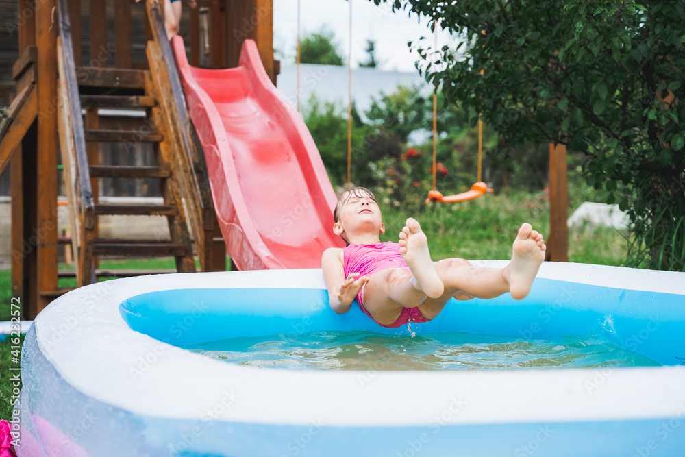 Staycation at home. Little girl in swimsuit rolls down slide into ...