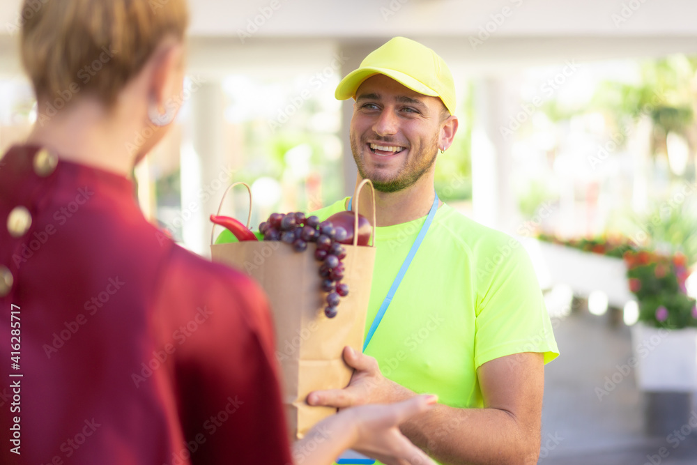 Handsome food delivery service man in yellow shirt holding fresh fruits ...