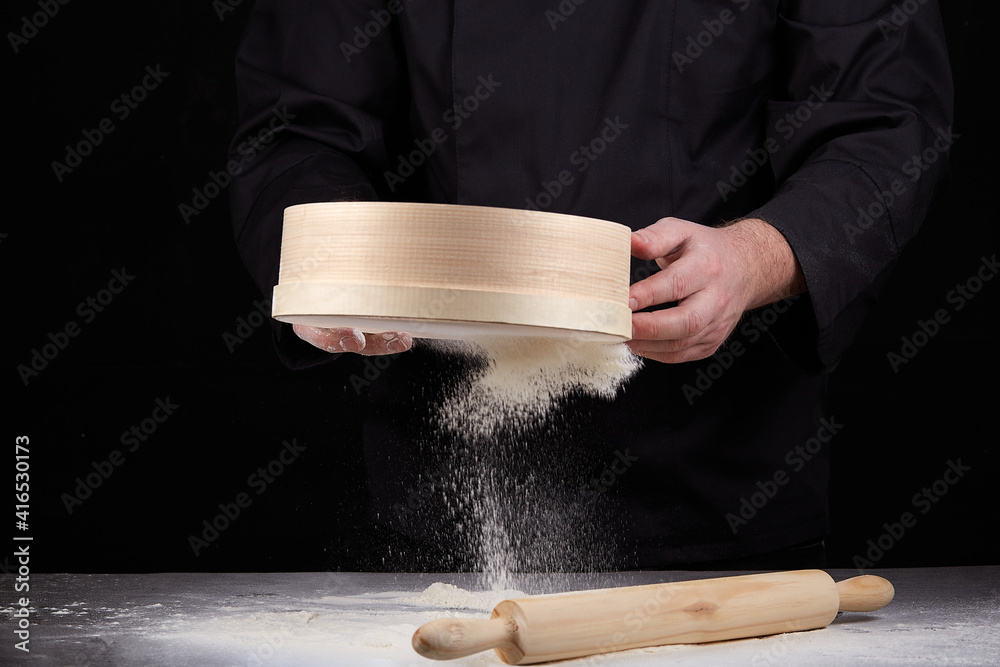 chef a man in a black uniform holds a round wooden sieve in his hands ...