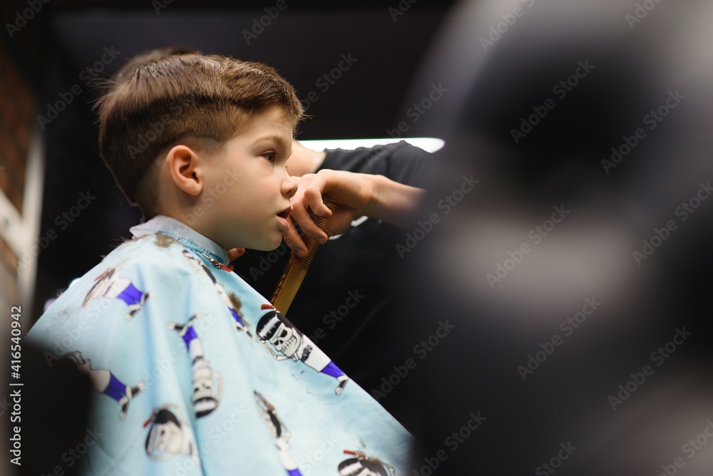 A little cute boy sits in a hairdresser's at the stylist's, a ...