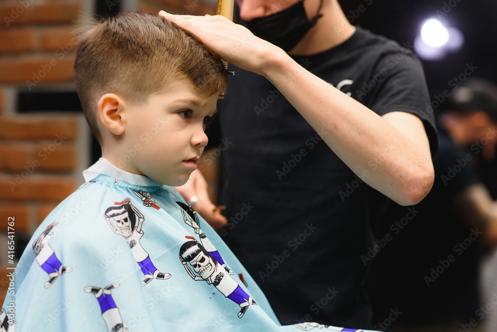 A little cute boy sits in a hairdresser's at the stylist's, a ...