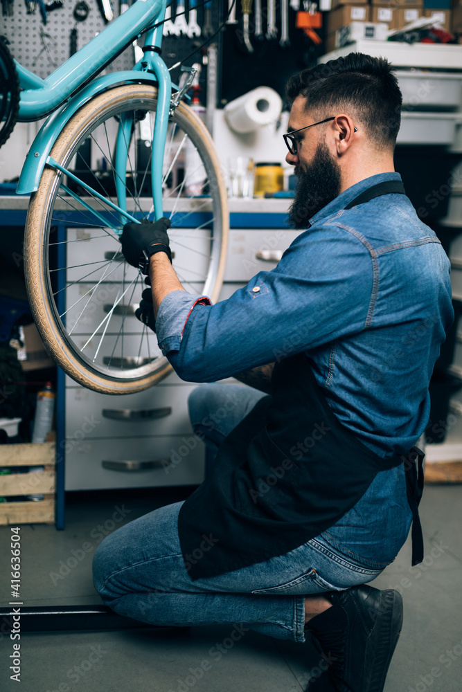 Young beard bicycle mechanic repairing bicycles in a workshop.. Stock ...