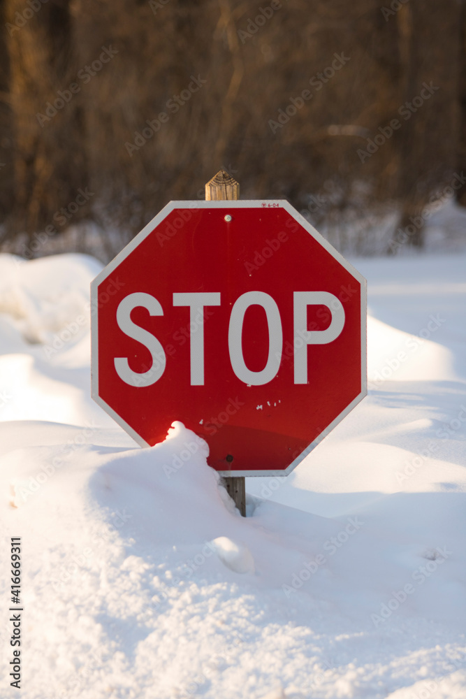 Snow reaching up to a red stop sign. Stock Photo | Adobe Stock