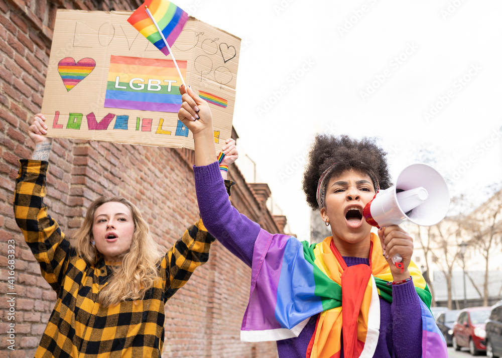 two multi-ethnic women celebrating gay pride event wearing the rainbow ...