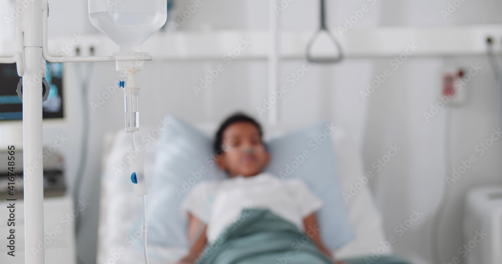 Focus on drip in hospital room with blurry patient child on hospital ...