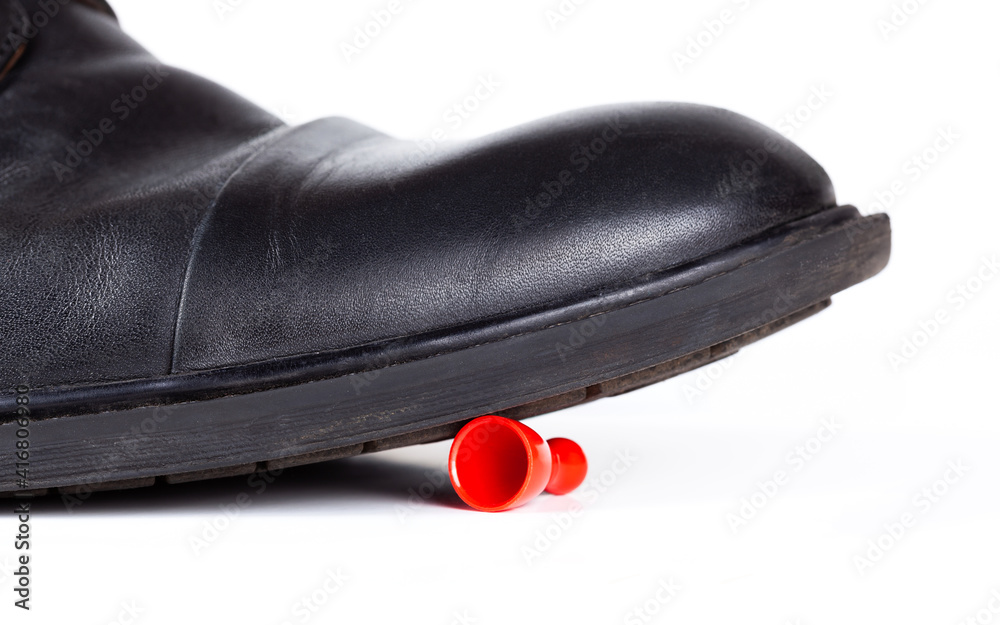 Big black boot crushing a small red game piece. Little object pinned ...