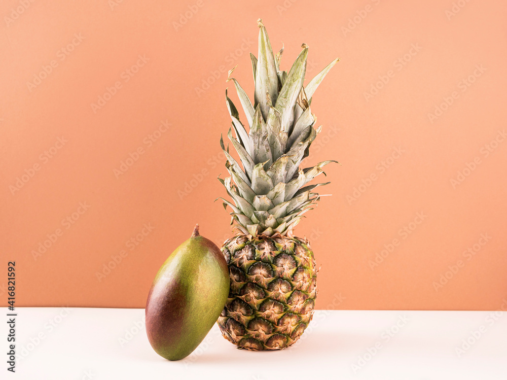 Ripe pineapples with mangoes, balancing fruit on a colored background ...