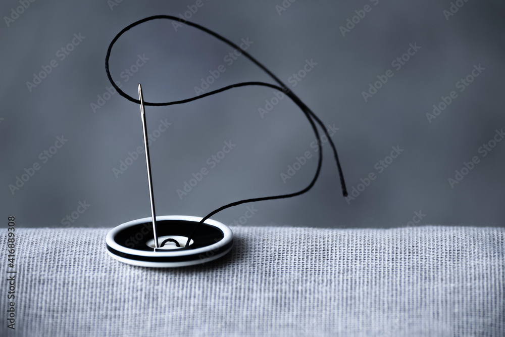 The black and white button is sewn with a sewing needle and black ...