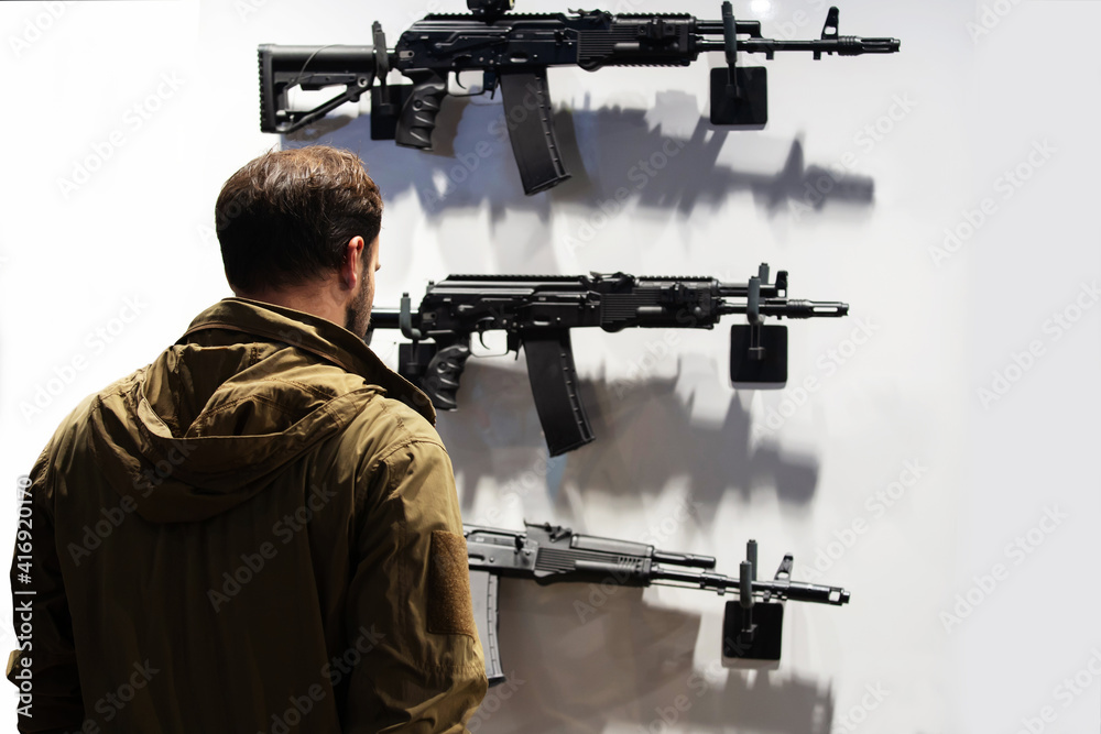 A man examines a stand with modern firearms. Machine guns of various ...