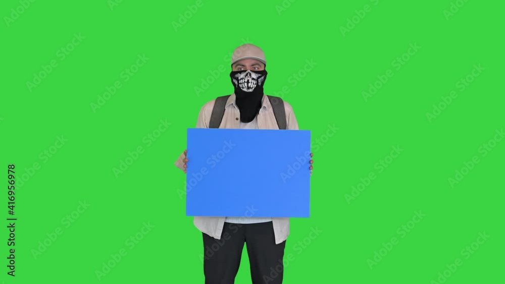 Young man protester with covered face holding blank board on a Green ...