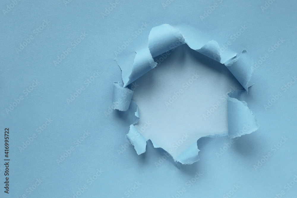 Paper hole with torn sides on a blue background. Through the paper. A ...