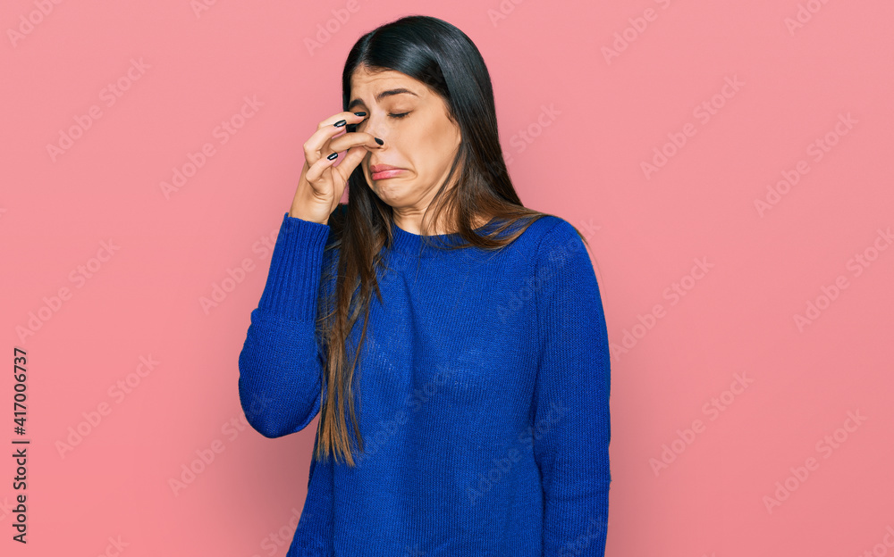 Young hispanic woman wearing casual clothes smelling something stinky ...