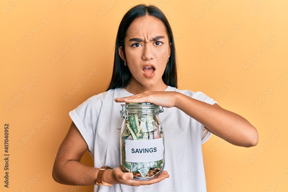 Young asian woman holding jar with savings in shock face, looking ...