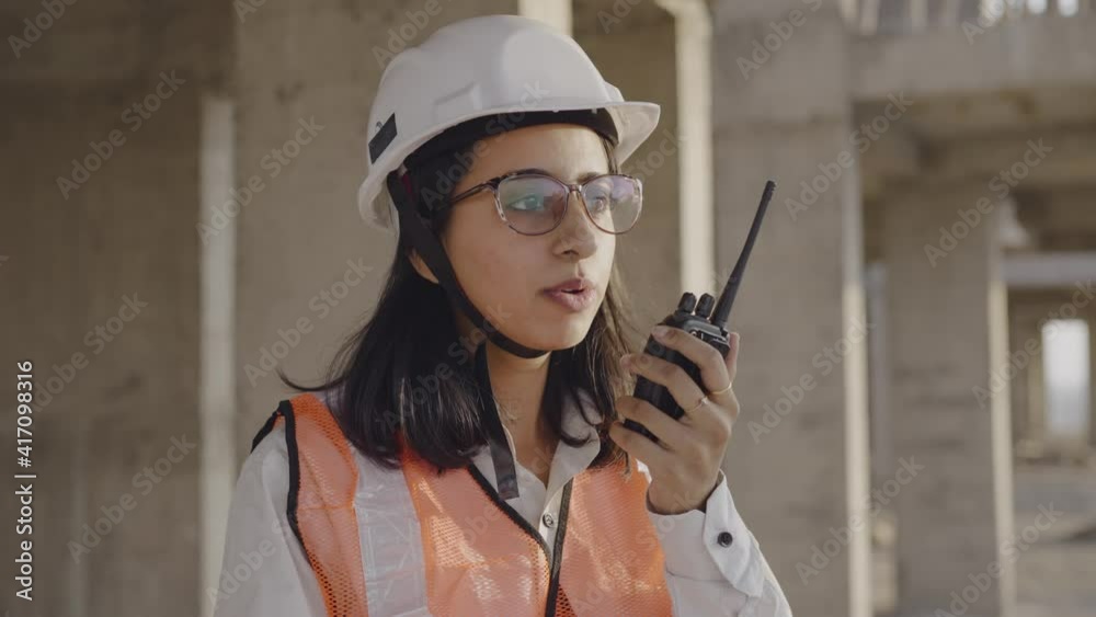 shot of young Indian female civil engineer speaking on a walkie talkie ...