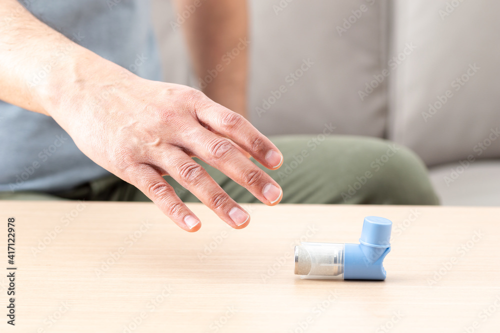Patient hand reaching blue asthma inhaler /COPD on wood table ...