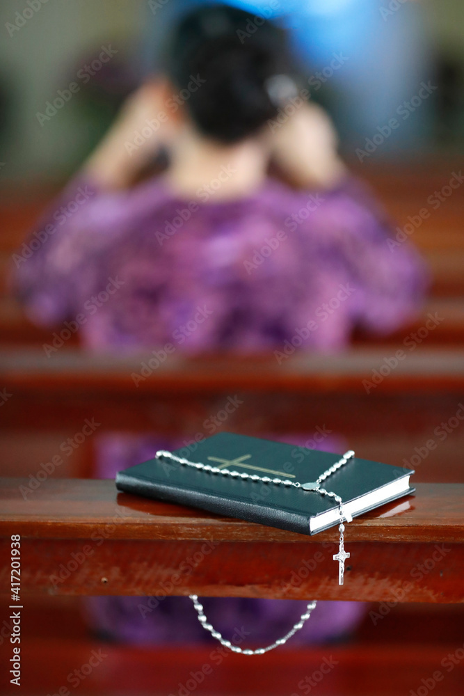 Woman praying and bible with rosary on a church bench. Basilica of Our ...