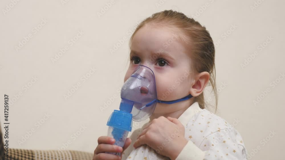 A cute baby in a mask is breathing through an inhaler. Home inhalation ...