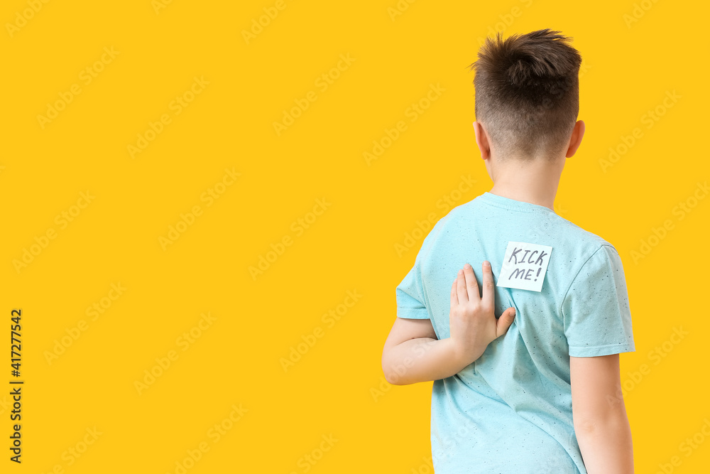 Sticky note with text KICK ME on back of little boy against color ...