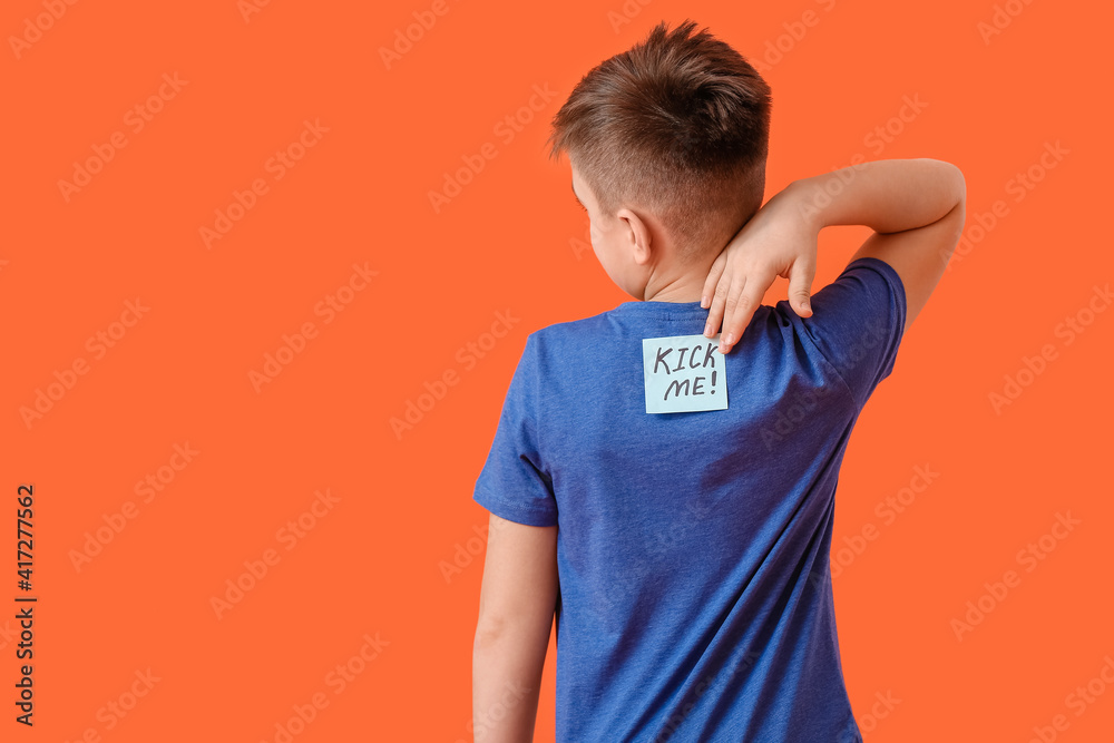 Sticky note with text KICK ME on back of little boy against color ...
