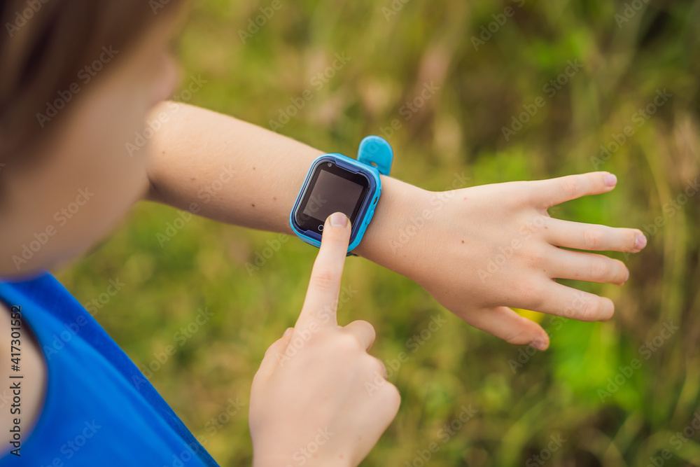 Boy uses kids smart watch outdoor against the background of the garden ...