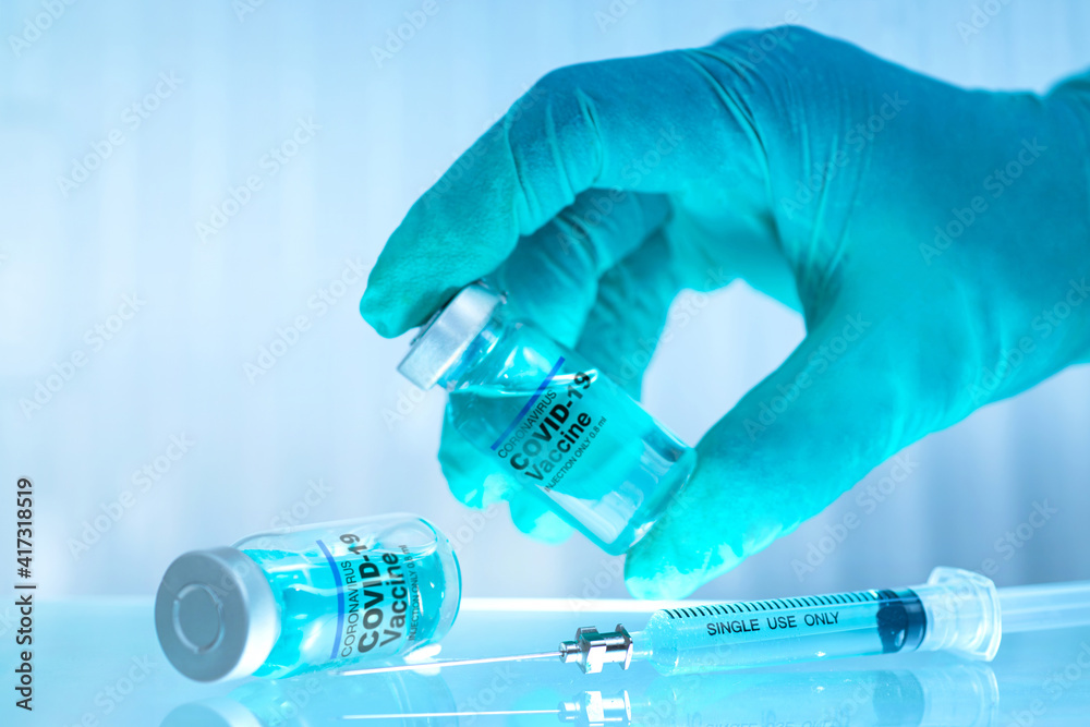 Hand of doctor wearing medial glove holding covid 19 corona virus vaccine vial bottle, and ...