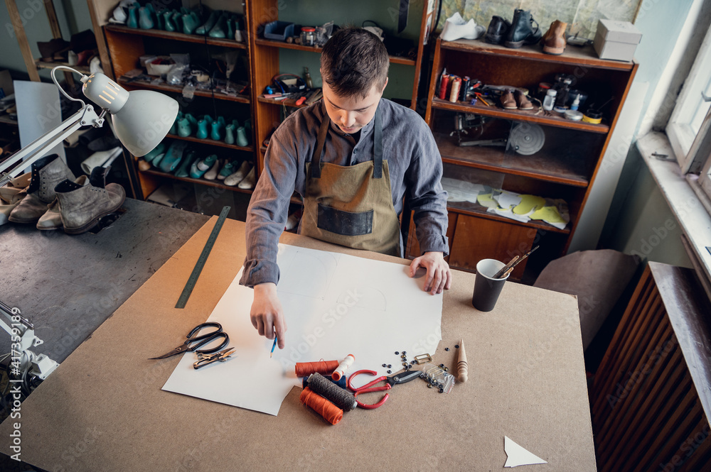An experienced shoemaker in a shoe production workshop makes a pattern ...