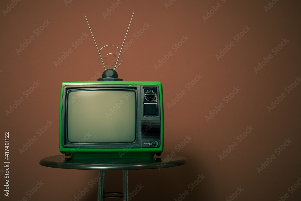 Old green TV with antenna on round table in front of the wall in a ...