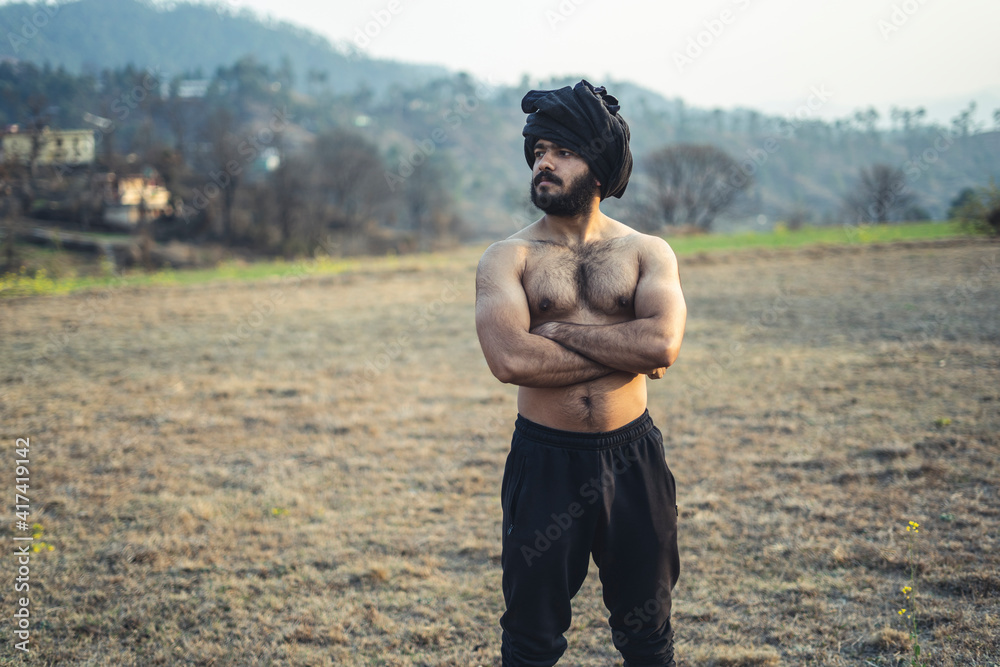 Young indian farmer with a turban standing on a wasteland field. Crops ...